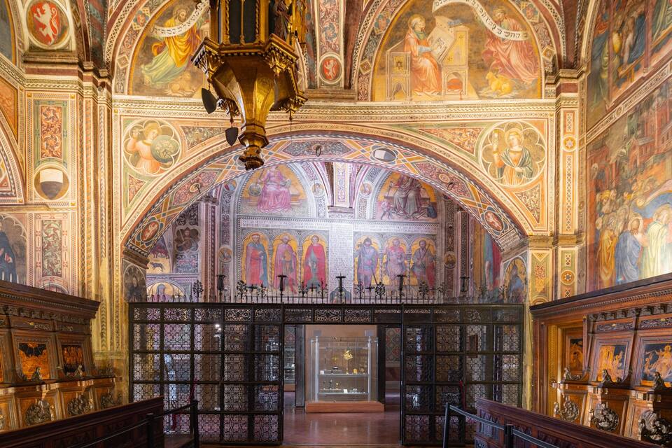 Interior de igreja com afrescos elaborados, altar central e disposição de bancos de madeira.