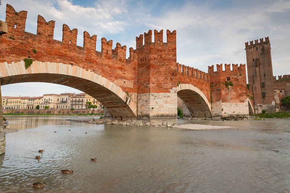 Uma ponte de pedra histórica sobre um rio, com um castelo ao fundo.