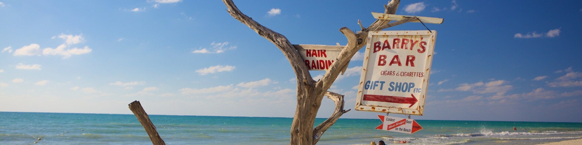 Uma praia com um letreiro indicando o Barry's Bar e uma loja de presentes.