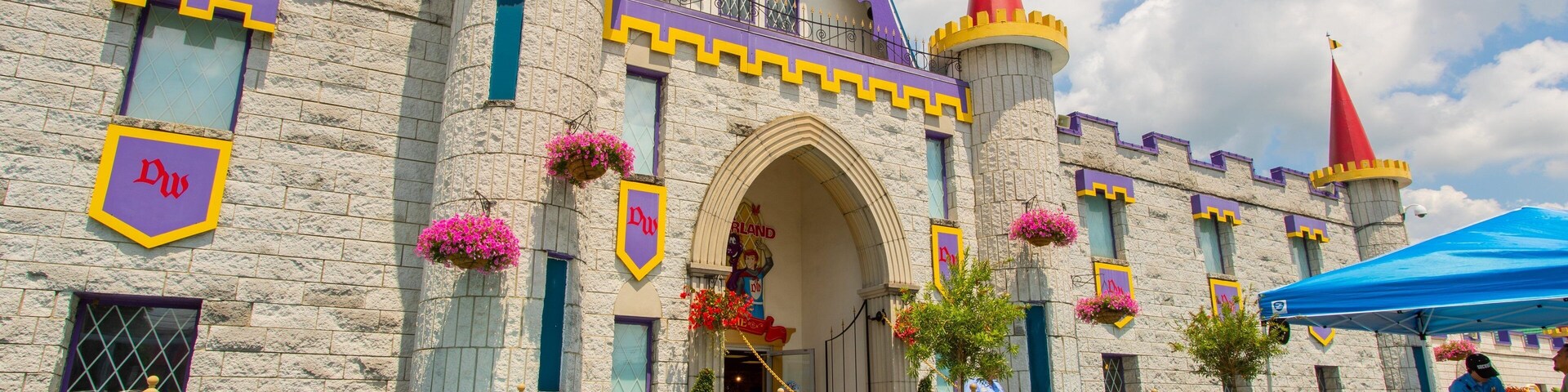Um edifício com estilo de castelo, fachada em roxo e amarelo, telhado pontudo vermelho e um letreiro com o logotipo 'DW'.