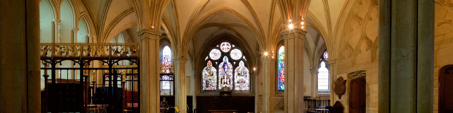 Interior de igreja com tetos abobadados, vitrais e fileiras de cadeiras.
