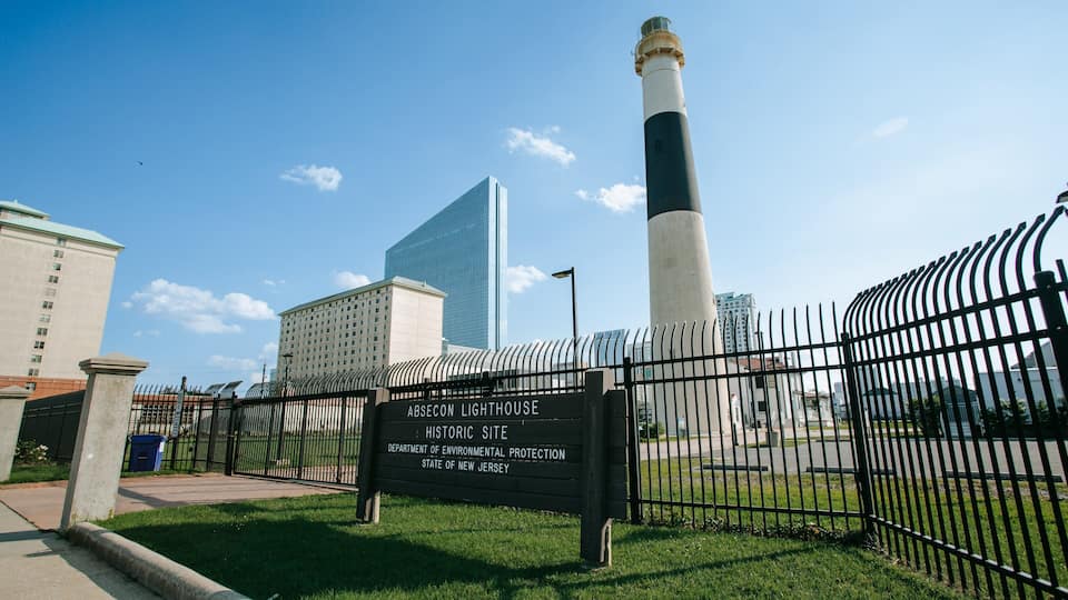 Sítio histórico com um farol, uma chaminé alta e edifícios modernos ao fundo.