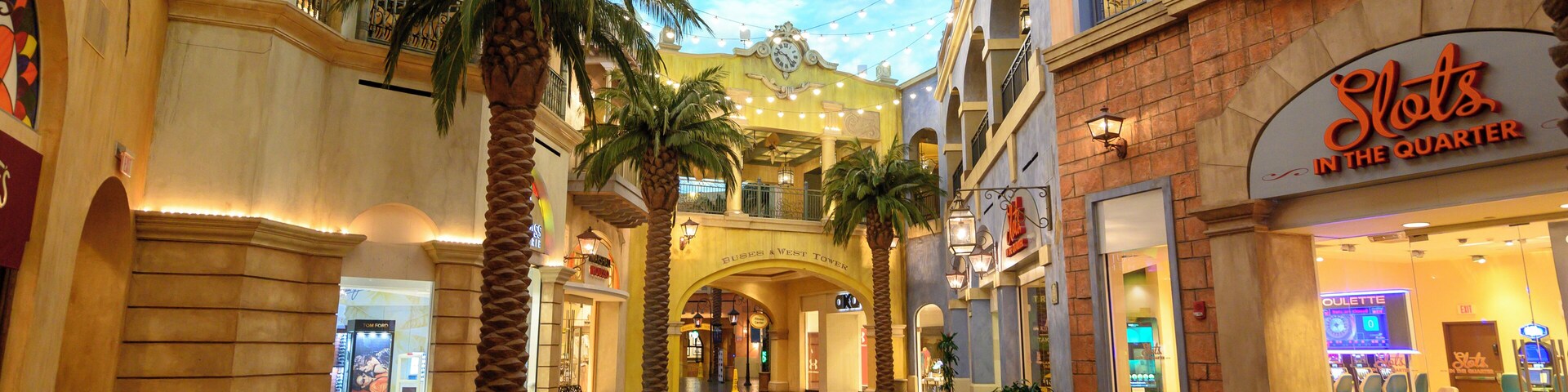 Um centro comercial com palmeiras, luzes de corda e uma placa com a inscrição 'Slots in the Quarter'.