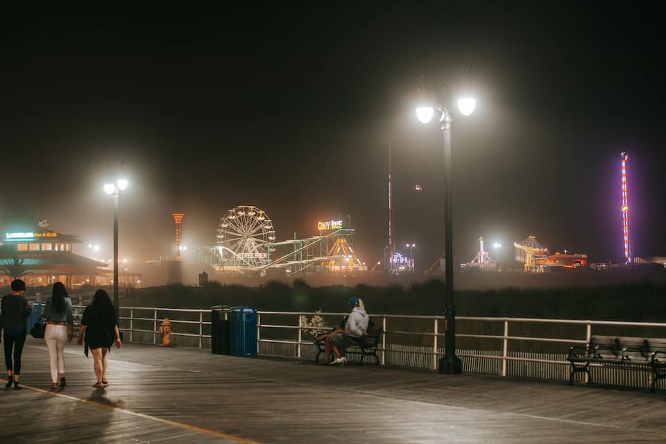Um calçadão à noite com uma roda gigante, uma montanha-russa e um edifício com letreiros neon.