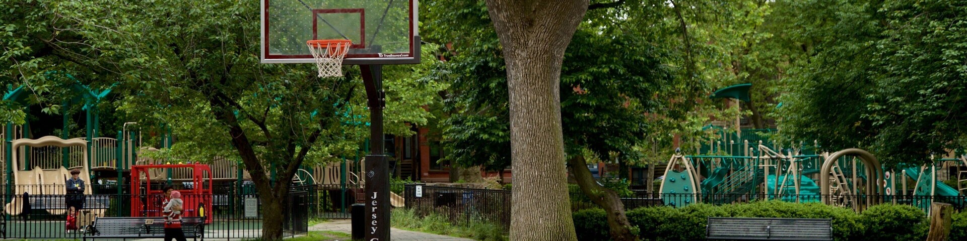 Uma quadra de basquete com um aro, cercada por árvores e equipamentos de recreação.