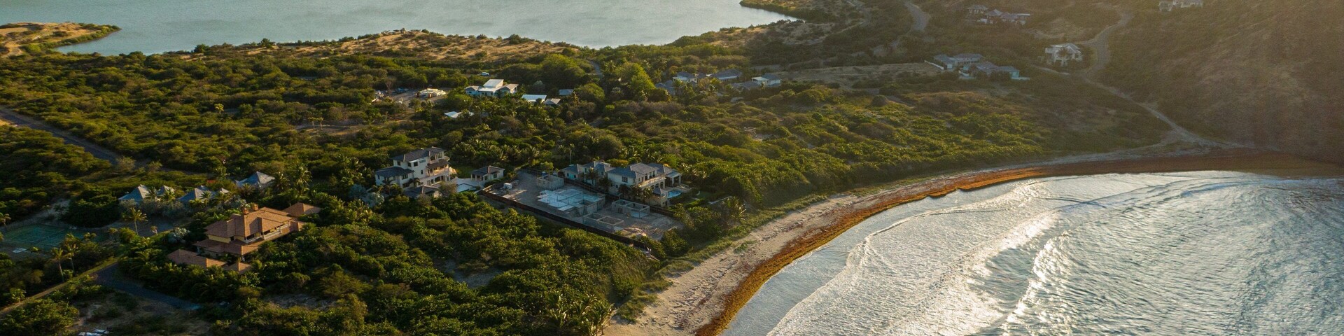 Paisagem costeira com praia, casas e uma baía com ilhas.