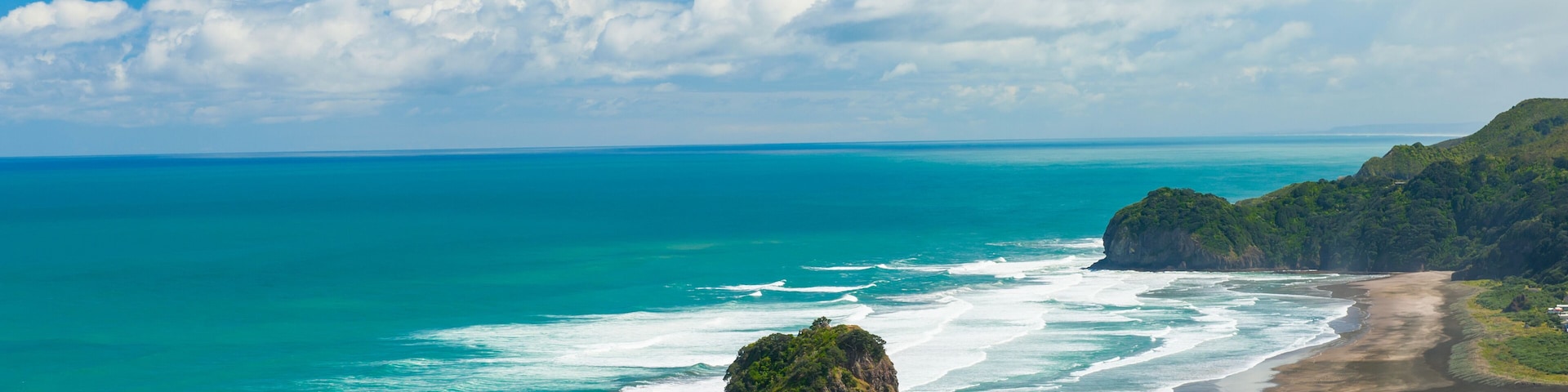 Paisagem costeira com um afloramento rochoso imponente, uma praia de areia e o oceano.