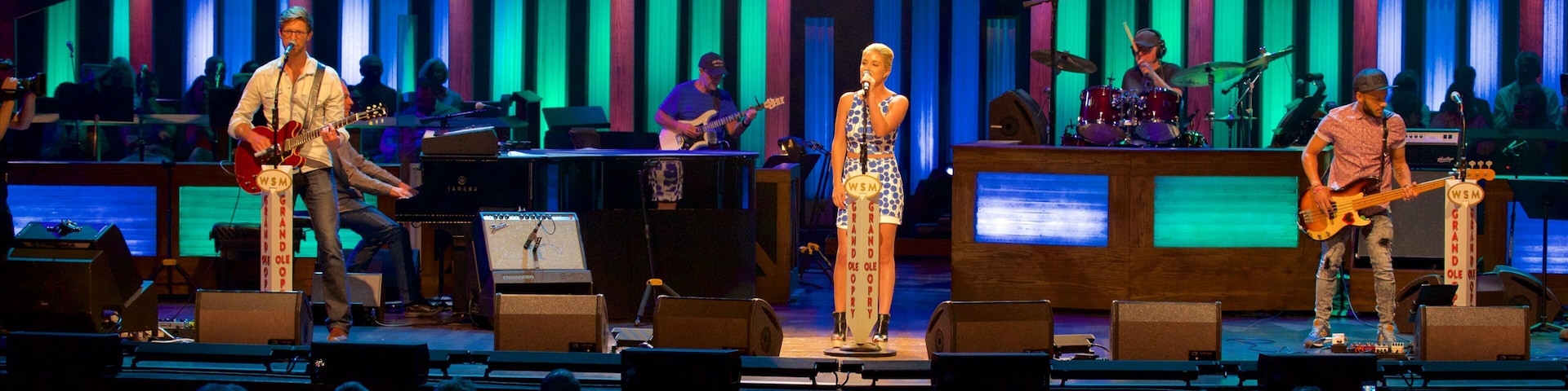 Apresentação de música ao vivo num palco, com uma multidão em primeiro plano.