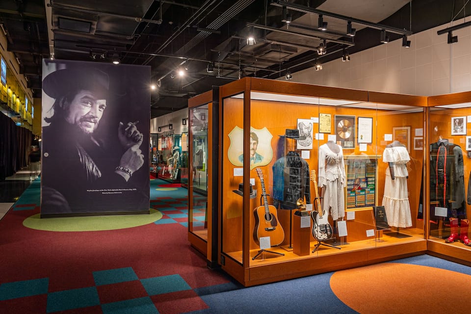 Uma exposição de museu com roupas antigas e guitarras.