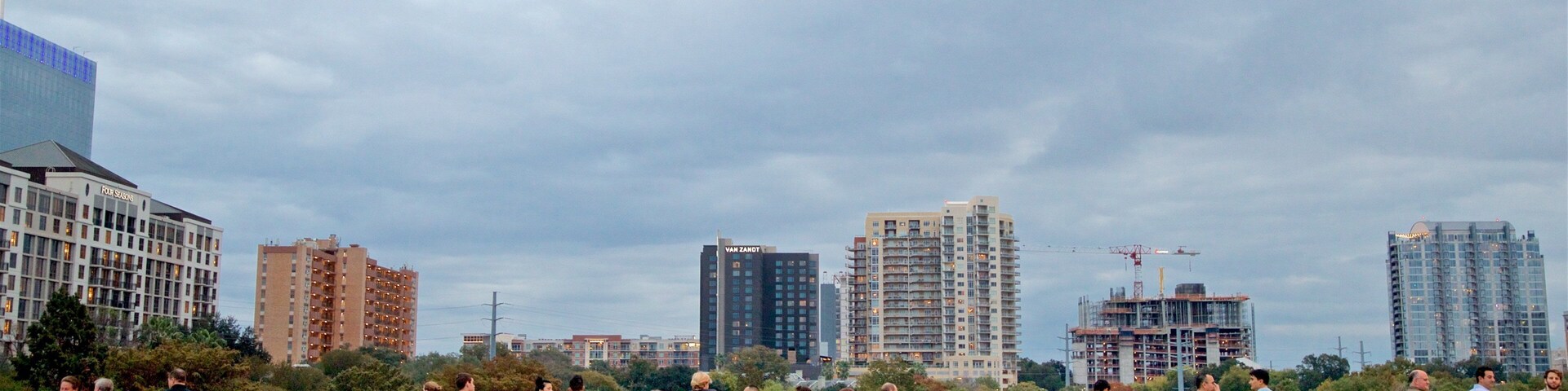 Uma ponte com pessoas em pé e sentadas, com vista para um horizonte urbano com diversos edifícios e um canteiro de obras.