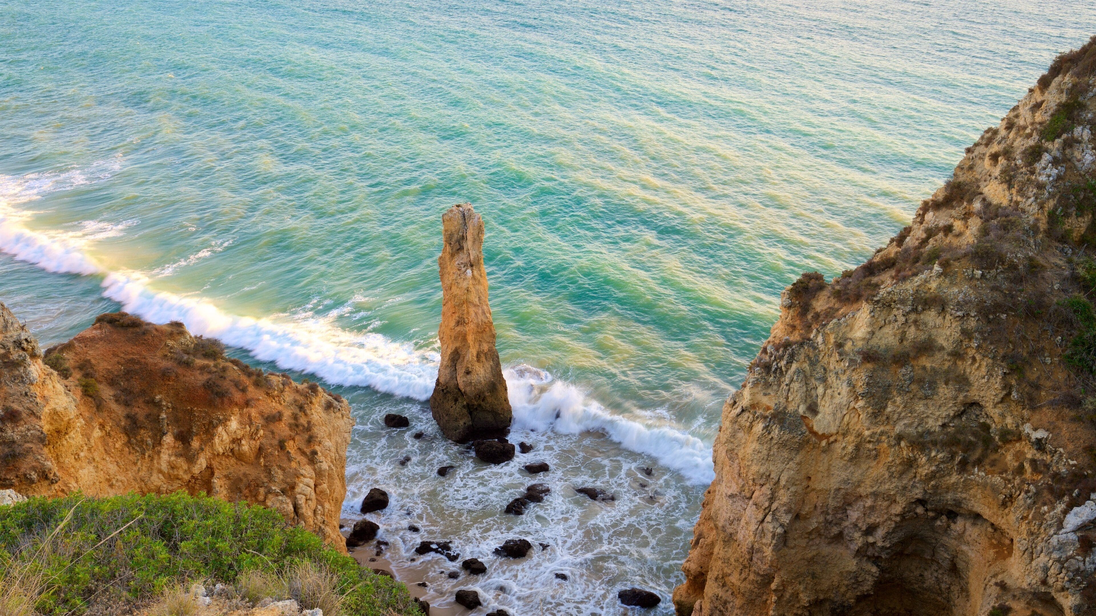 Paisagem costeira com uma formação rochosa imponente, rodeada por falésias e o oceano.