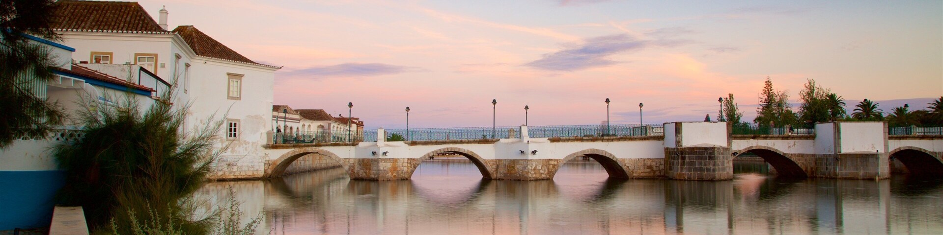 Um rio calmo com pontes de pedra e um edifício branco com detalhes azuis.