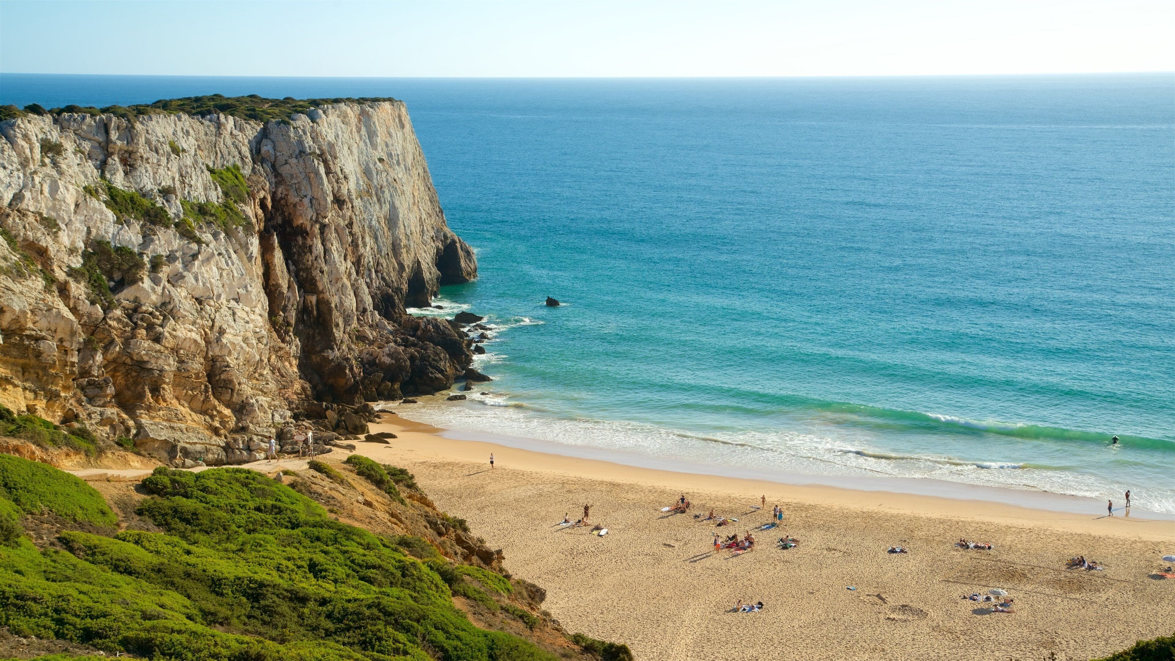 Paisagem costeira com uma praia arenosa, falésias rochosas e o oceano.