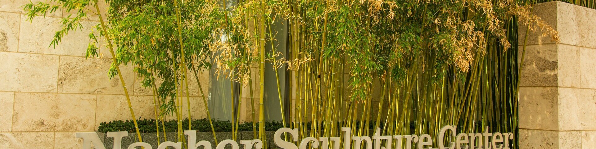 Um jardim de esculturas com bambus altos e um muro de pedra.