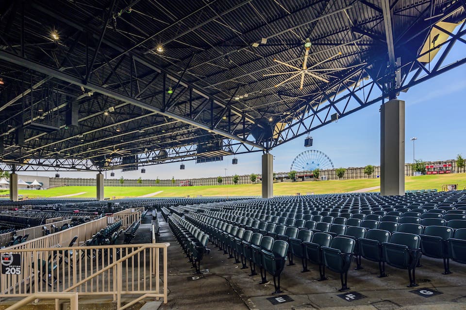 Um estádio vazio com fileiras de assentos, um amplo telhado metálico e uma roda gigante ao fundo.