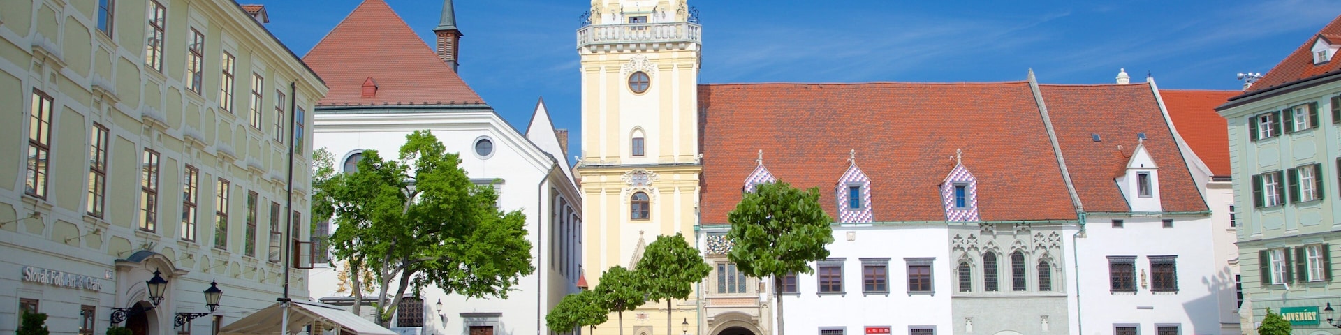Uma praça com uma torre de relógio, edifícios históricos e uma fonte.