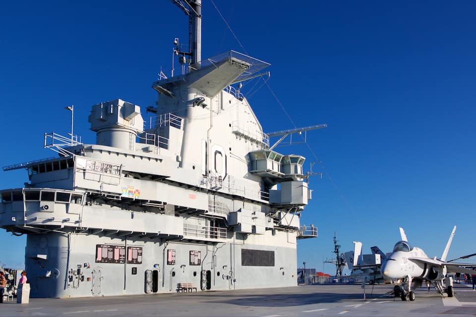 Um grande navio de guerra com um helicóptero e um caça no convés.