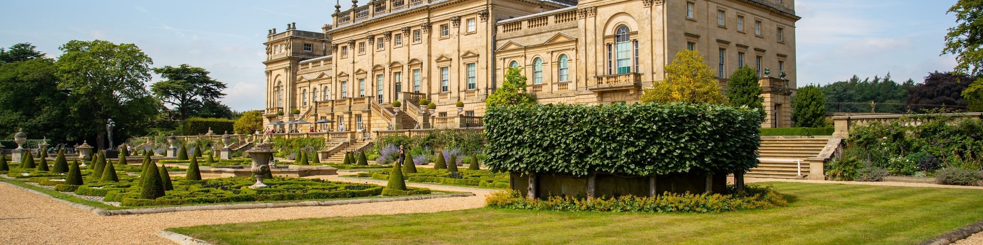 Um edifício grande e histórico com um jardim formal e gramados bem cuidados.