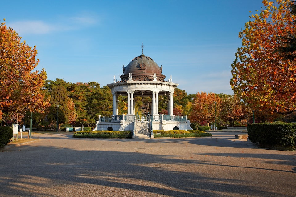Um gazebo com teto abobadado, rodeado por árvores com folhas de outono.