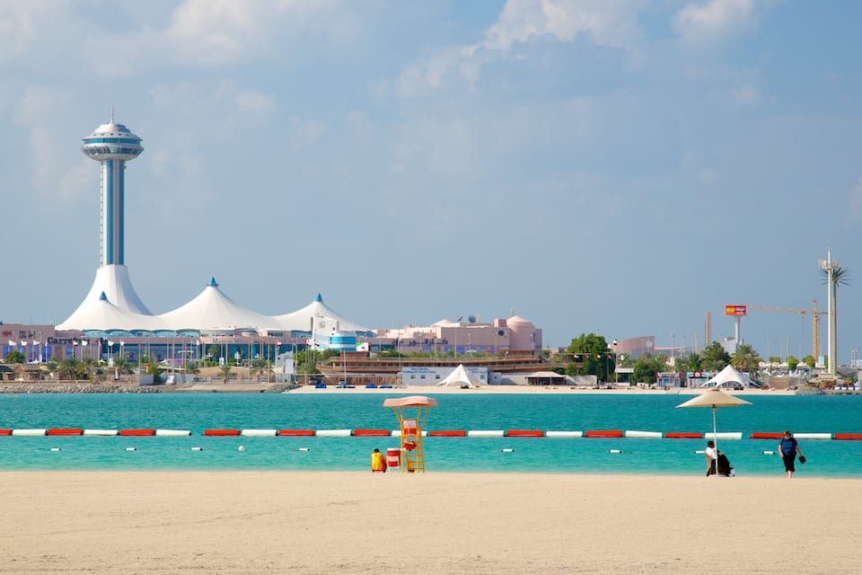 Uma praia com uma torre, guarda-sóis e um porto de recreio.
