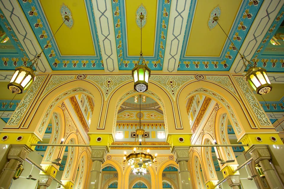 Um interior ricamente decorado, com arcos ornamentados, lustres e padrões complexos no teto.