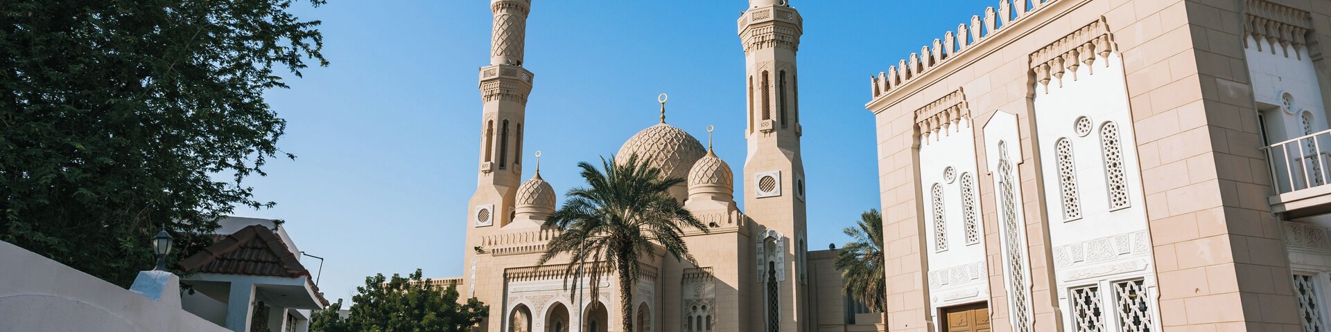 Uma mesquita com duas minaretes e uma grande cúpula, cercada por uma rua com carros e pedestres.