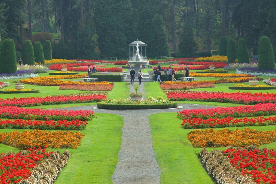 Um jardim formal com uma fonte central, canteiros florais simétricos e sebes bem aparadas.