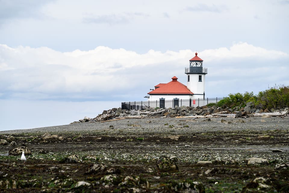 Um farol numa costa rochosa, com telhado vermelho e torre branca.