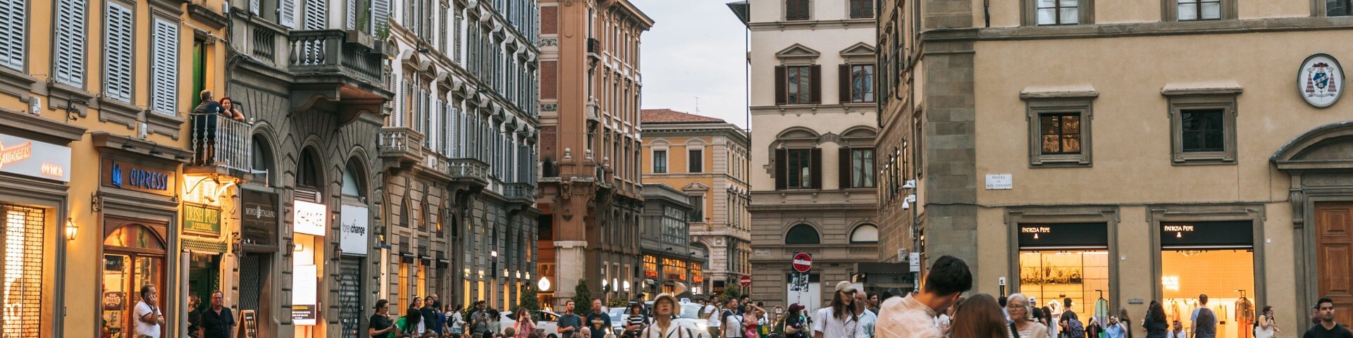 Uma rua movimentada com edifícios históricos, cafés ao ar livre e pessoas caminhando.
