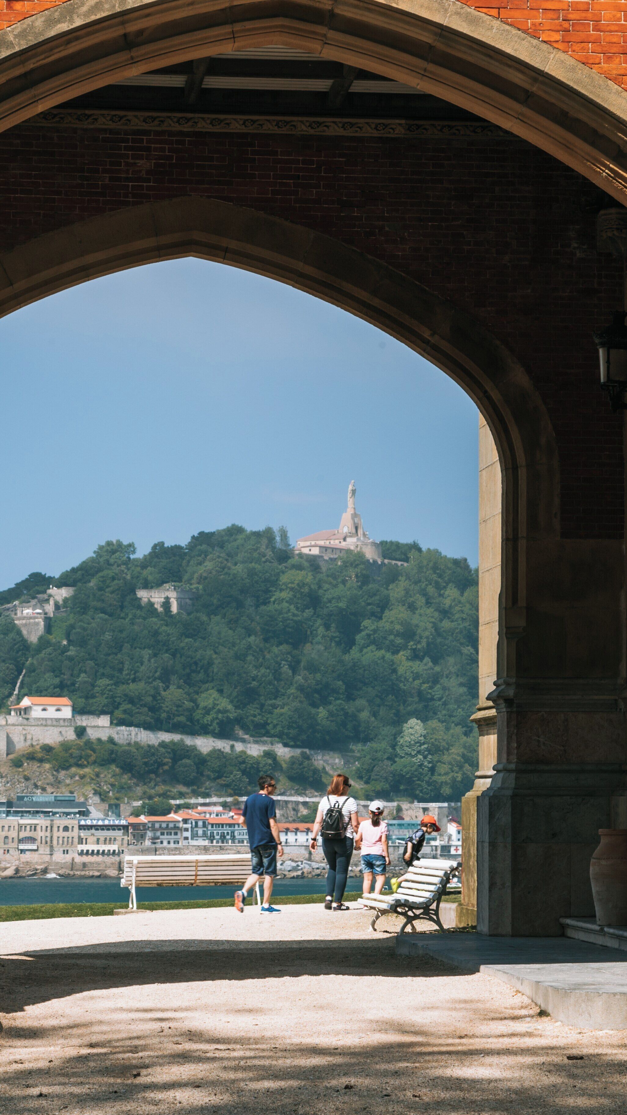 Visitors stroll through a stunning archway at Miramar Palace overlooking the scenic hills of San Sebastián in Basque Country, Spain on a clear sunny day