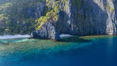 Paisagem costeira com águas turquesa cristalinas, falésias rochosas e uma praia arenosa.