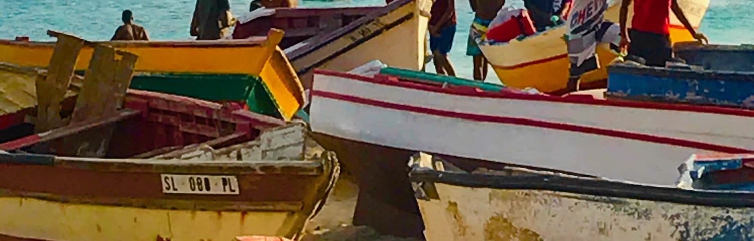 Vários barcos pequenos atracados num cais, com pessoas em cima.