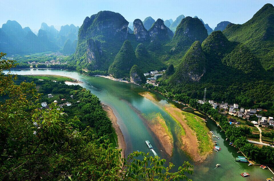 Um rio serpenteando por uma paisagem montanhosa, com vegetação exuberante e algumas embarcações.