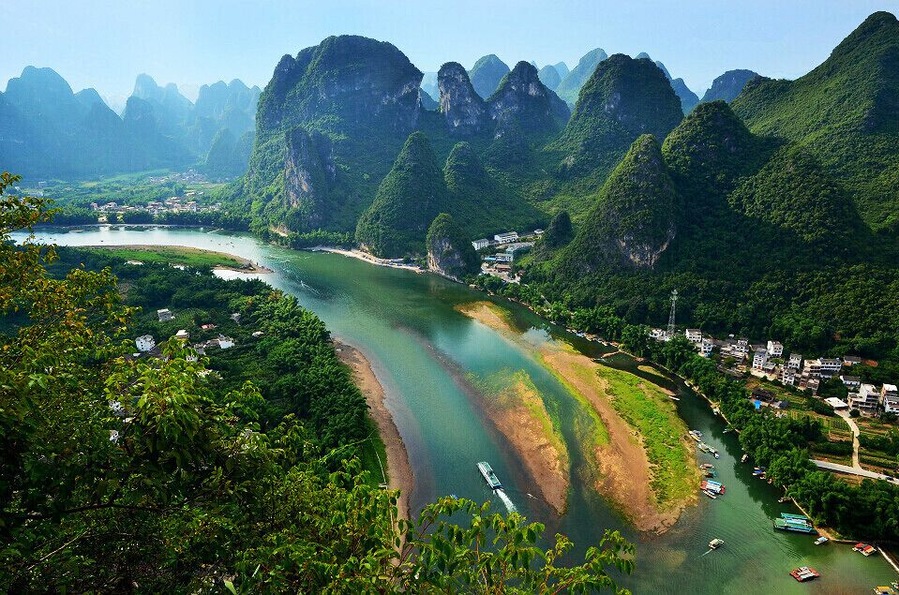 Um rio serpenteando por uma paisagem montanhosa, com vegetação exuberante e algumas embarcações.