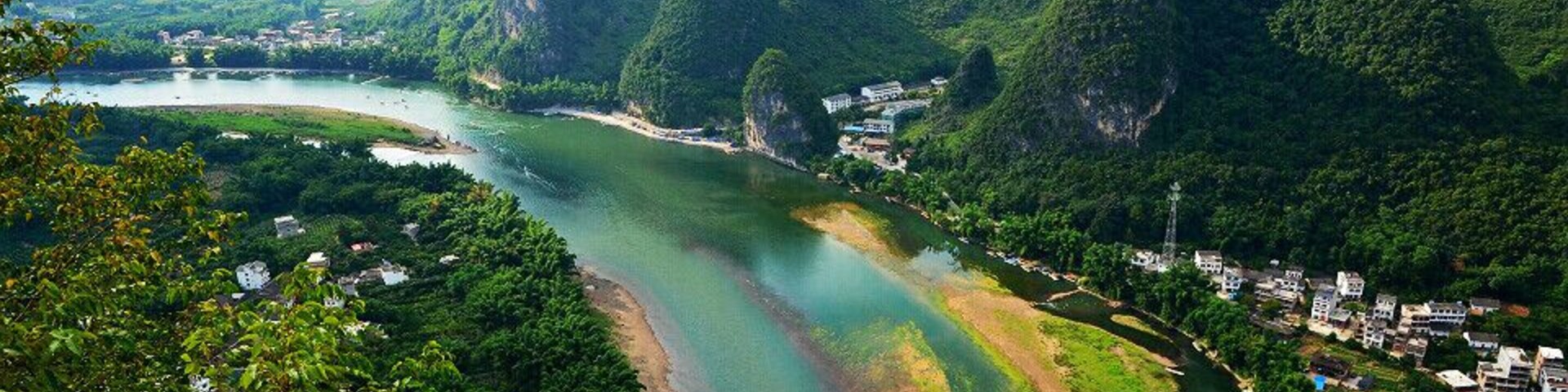 Um rio serpenteando por uma paisagem montanhosa, com vegetação exuberante e algumas embarcações.