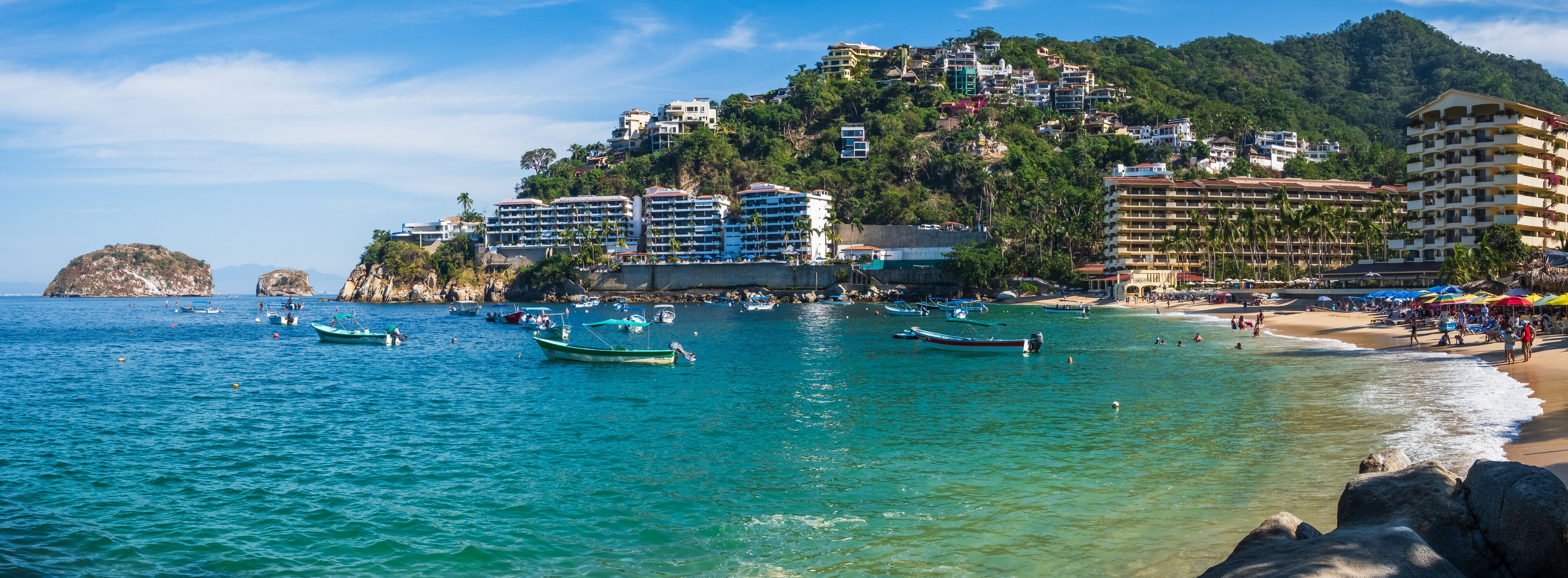 Uma vila costeira com praia, barcos e edifícios numa encosta.