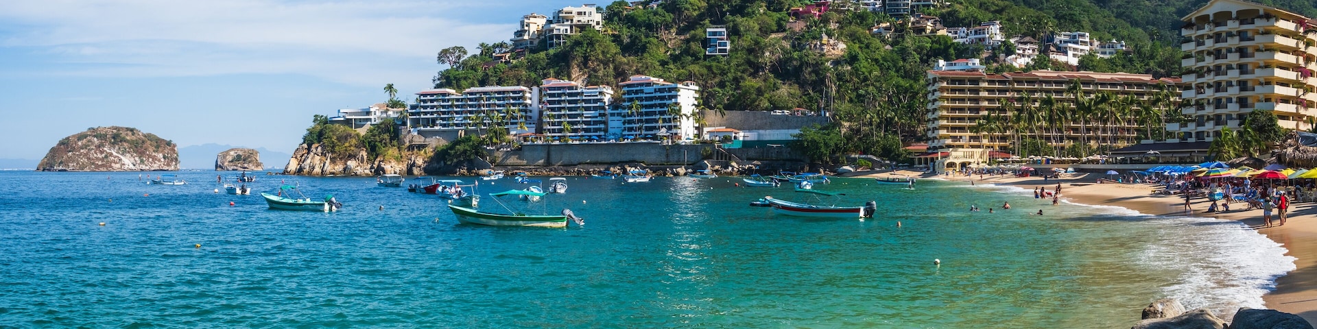Uma vila costeira com praia, barcos e edifícios numa encosta.