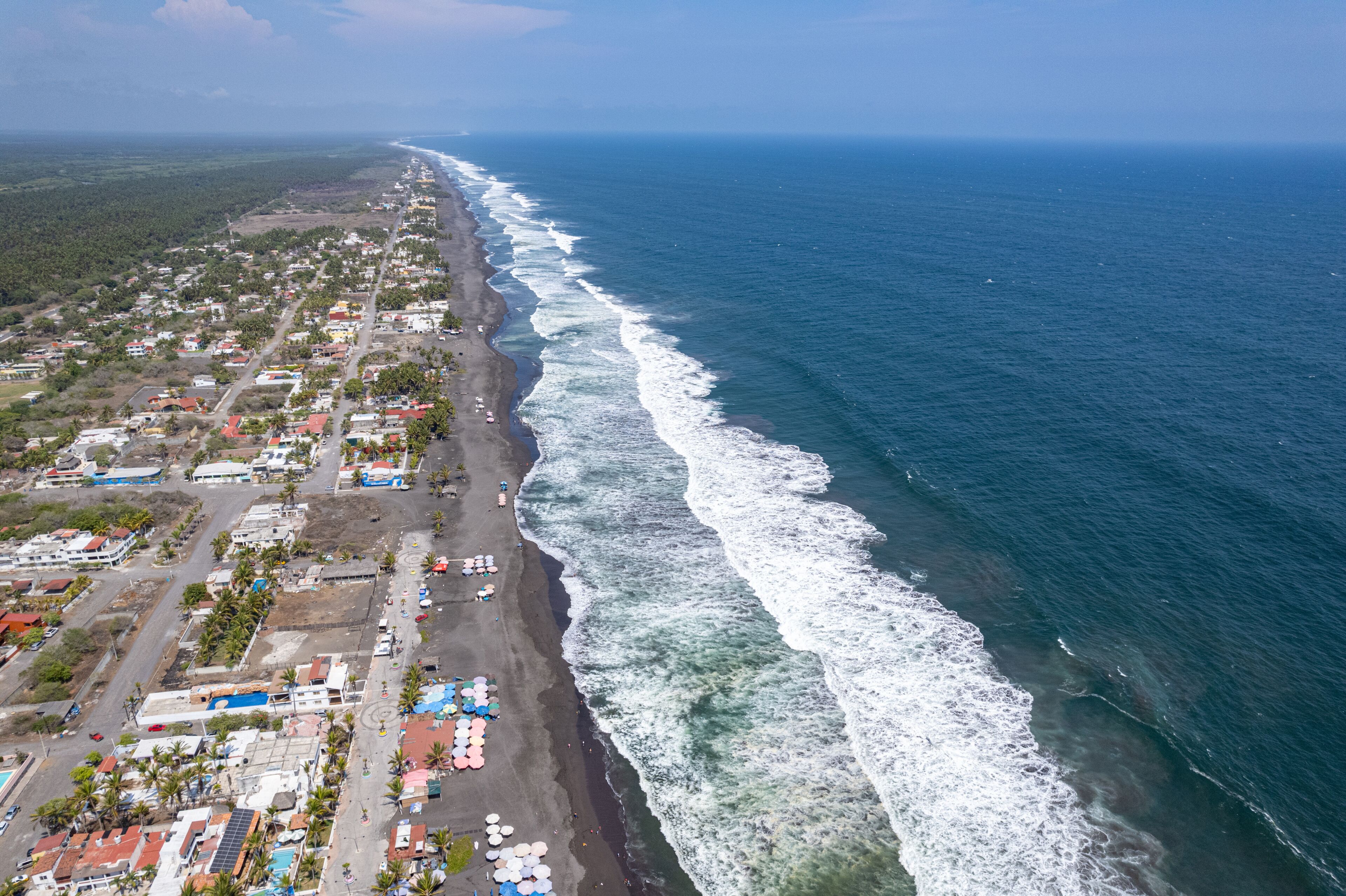 Vista aérea de uma cidade costeira com praia, ondas do oceano e edifícios residenciais.