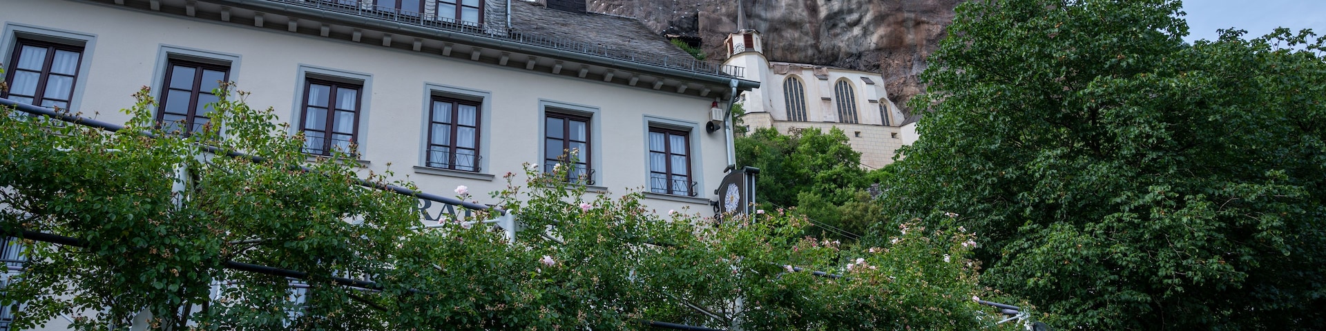 Um edifício com uma torre do relógio, uma grande formação rochosa e árvores verdes exuberantes.