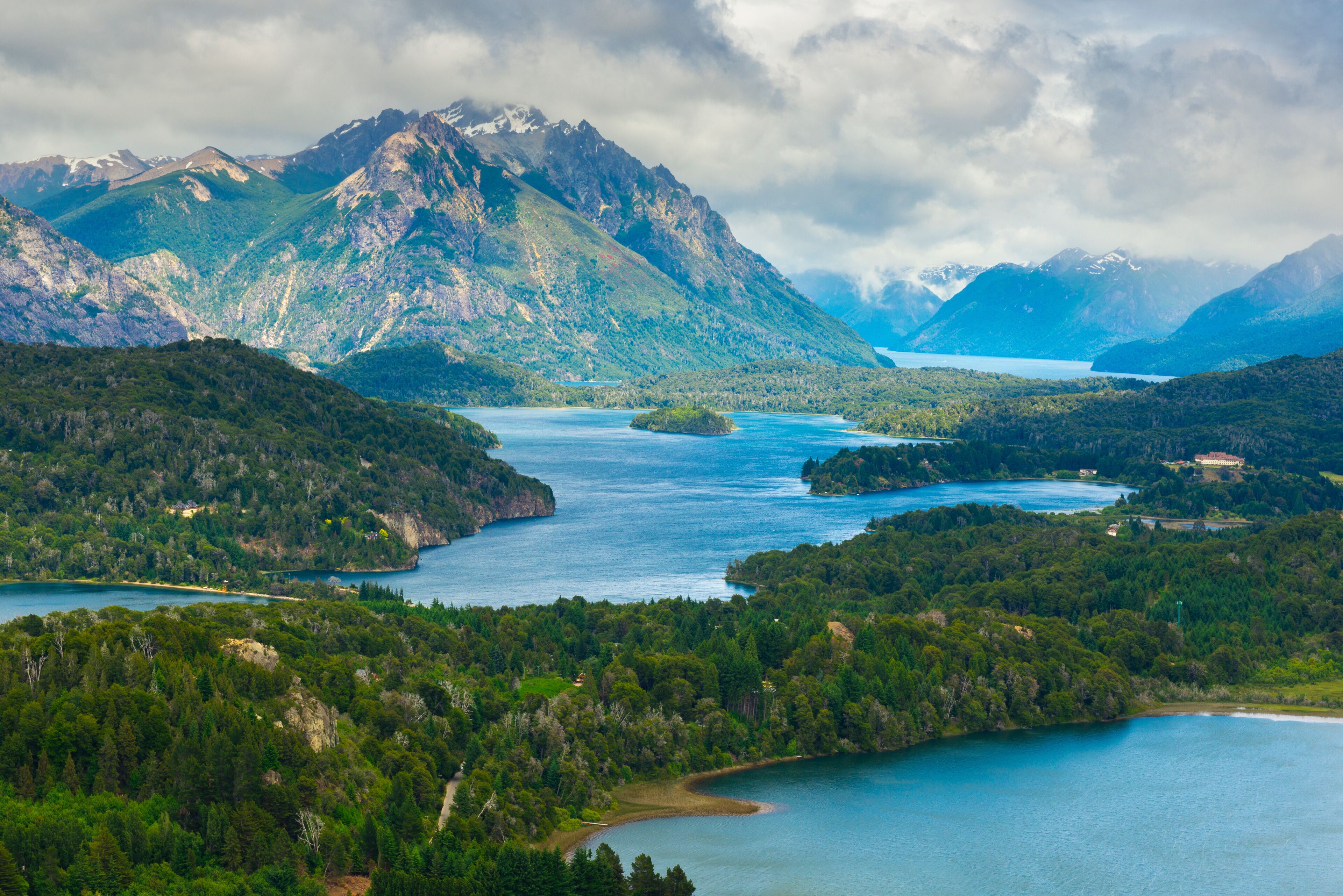 Paisagem montanhosa com um lago rodeado por florestas densas e uma cordilheira ao longe.