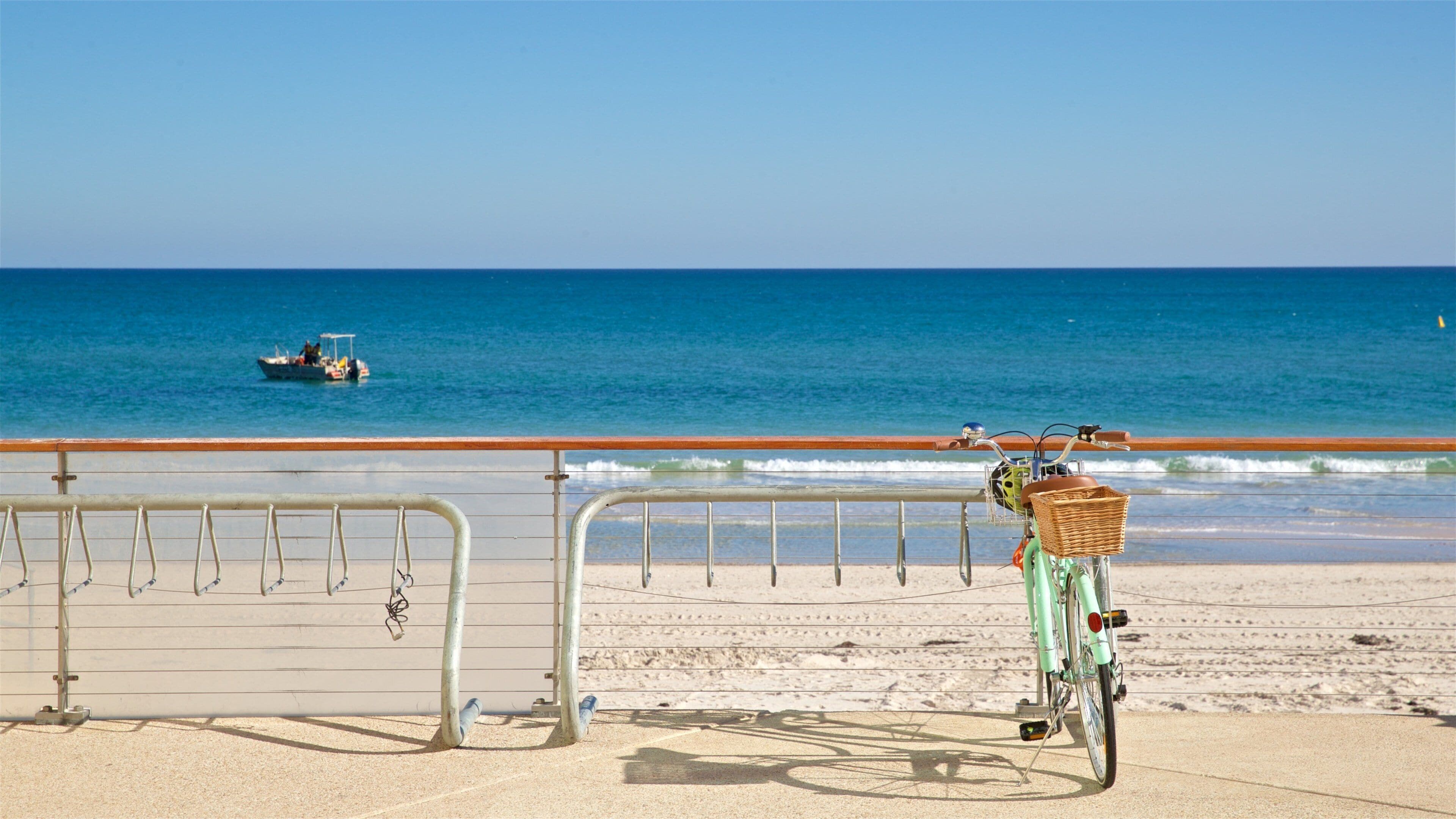 Uma praia com uma bicicleta, um corrimão e um barco na água.