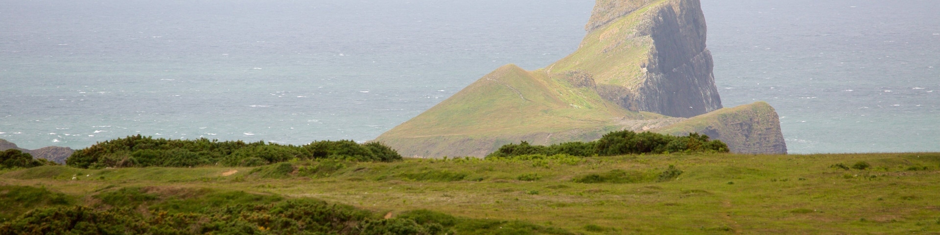 Paisagem costeira com uma formação rochosa imponente e vegetação exuberante.