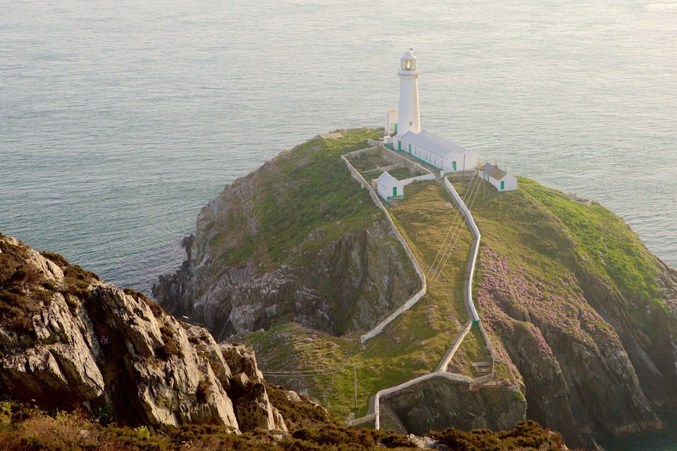 Um farol numa ilha rochosa, rodeada por um mar calmo.