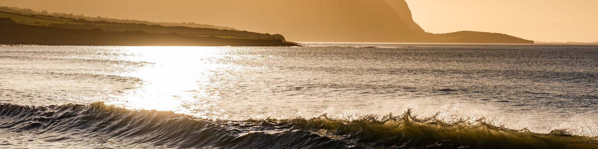 Paisagem costeira com ondas, uma cordilheira e um pôr do sol.