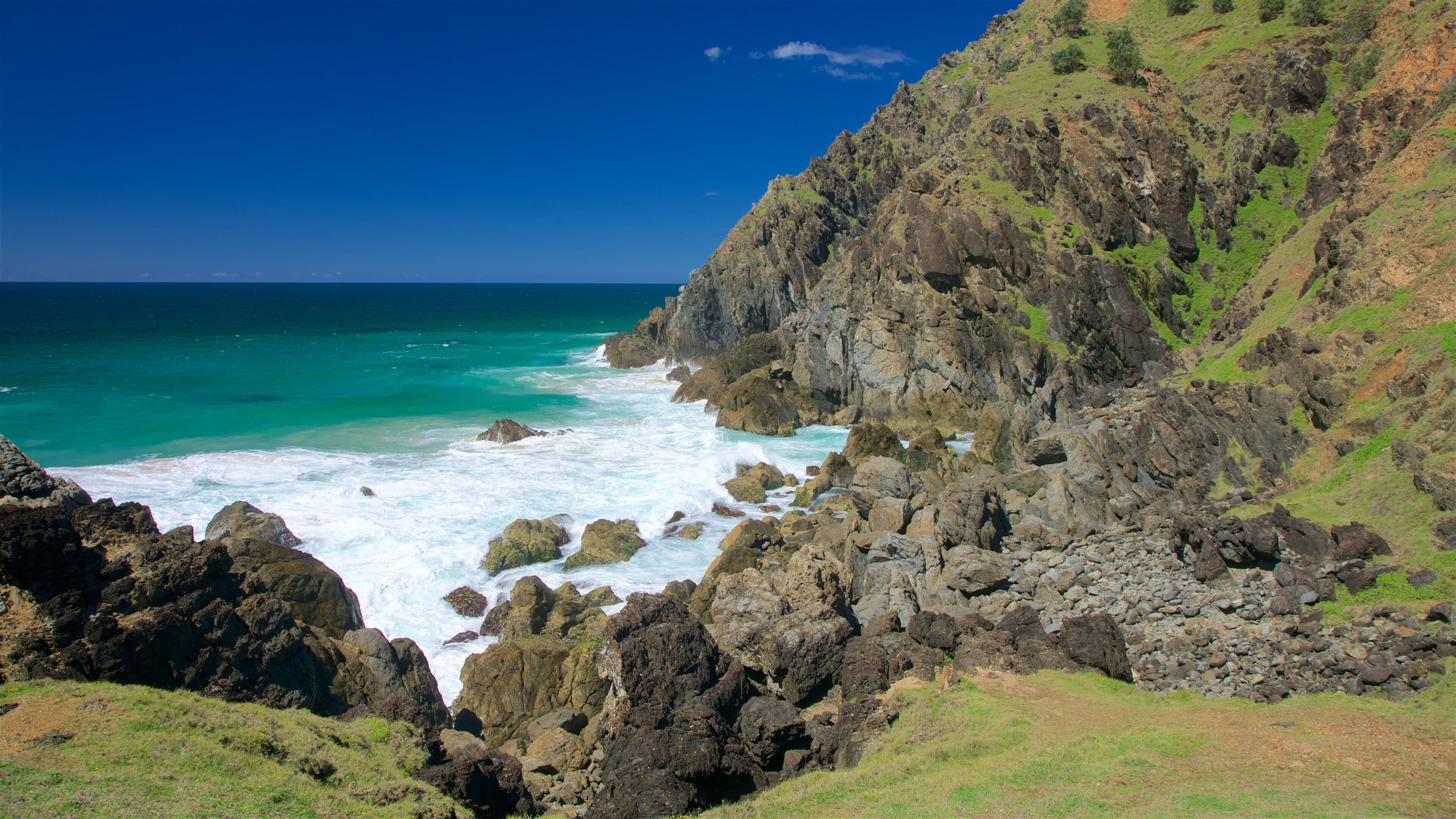Litoral acidentado com falésias rochosas e ondas oceânicas azul-turquesa quebrando nas rochas.