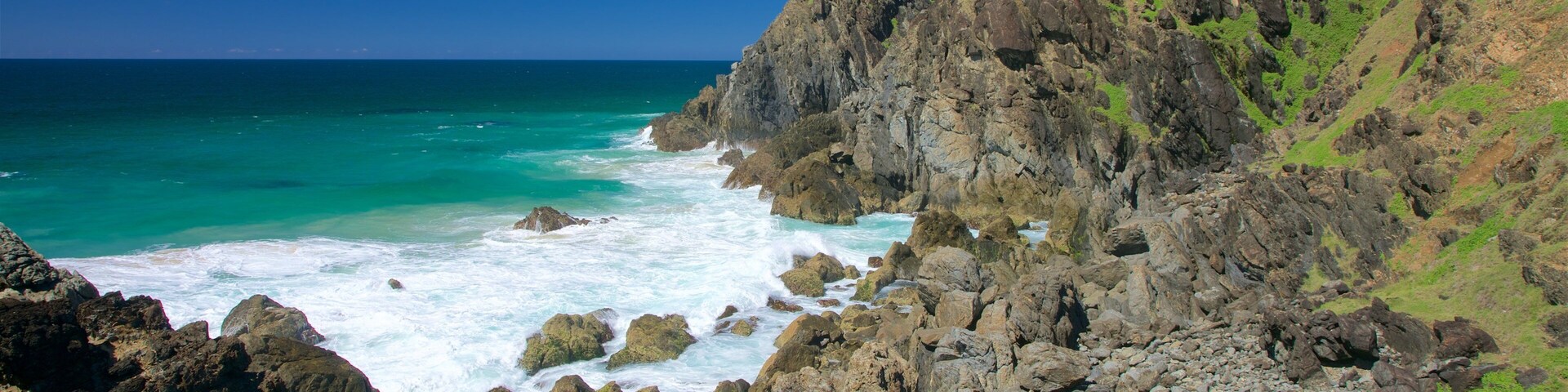 Litoral acidentado com falésias rochosas e ondas oceânicas azul-turquesa quebrando nas rochas.