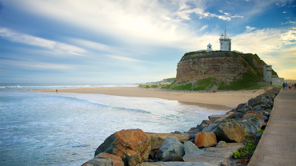 Cena costeira com um farol em um penhasco, uma praia de areia e um molhe rochoso.