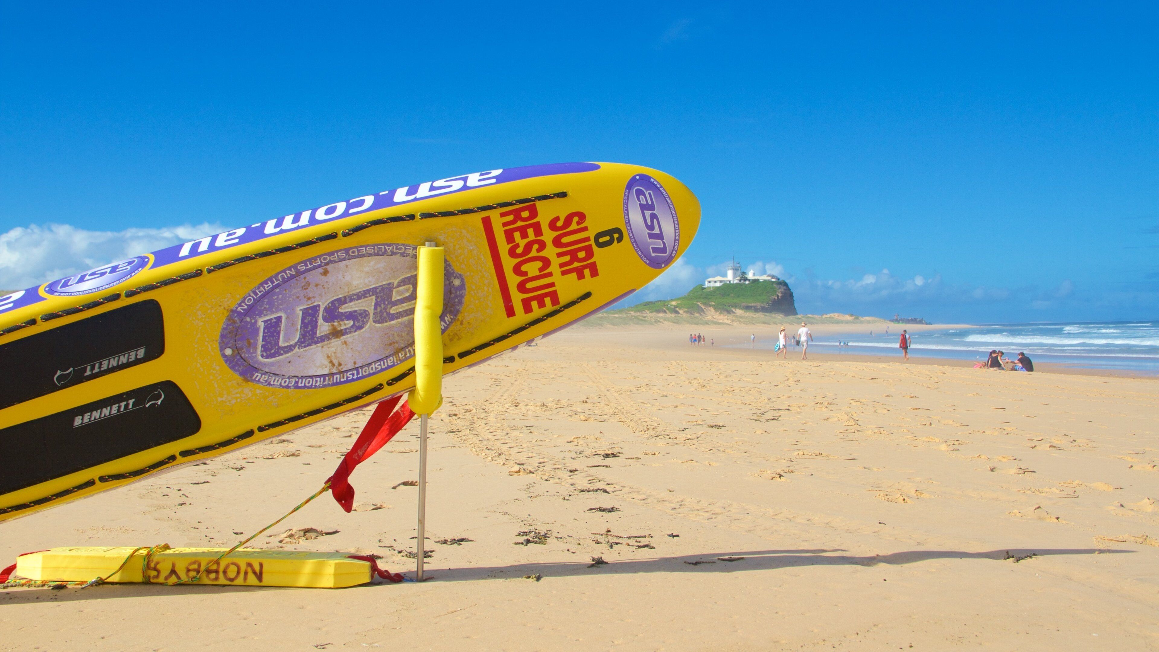 Uma boia de resgate amarela na praia, com pessoas ao fundo.
