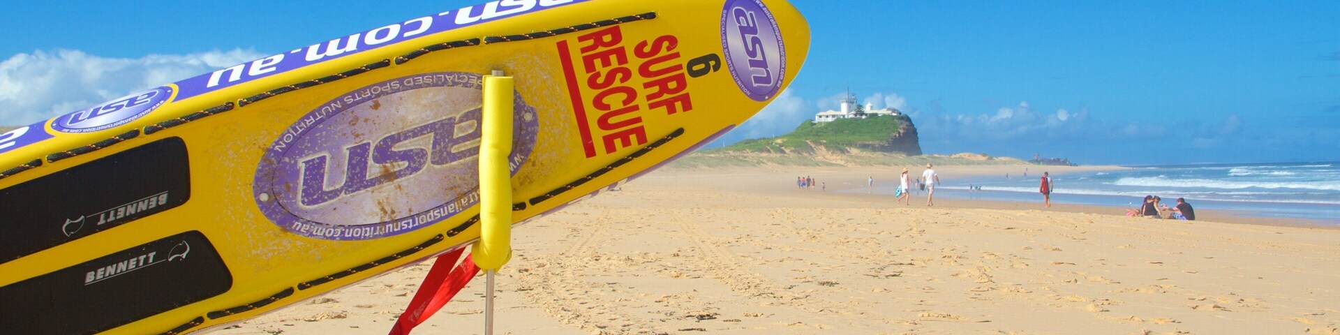 Uma boia de resgate amarela na praia, com pessoas ao fundo.