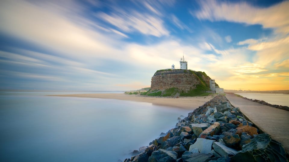 Um farol costeiro numa rocha com mar calmo e céu claro.